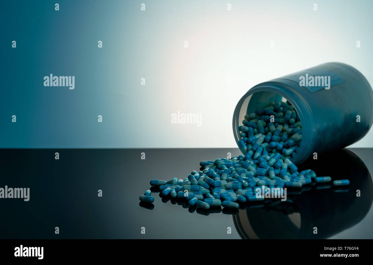 Blue and white capsule pill spilled out from white plastic bottle ...