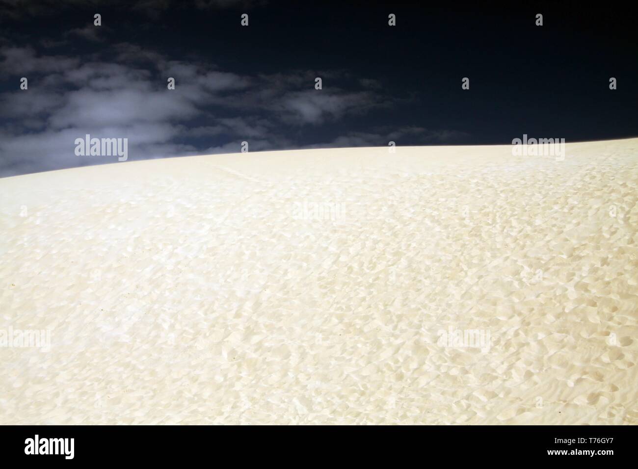 Bright shining white edge of sand dune contrasting against deep blue ...