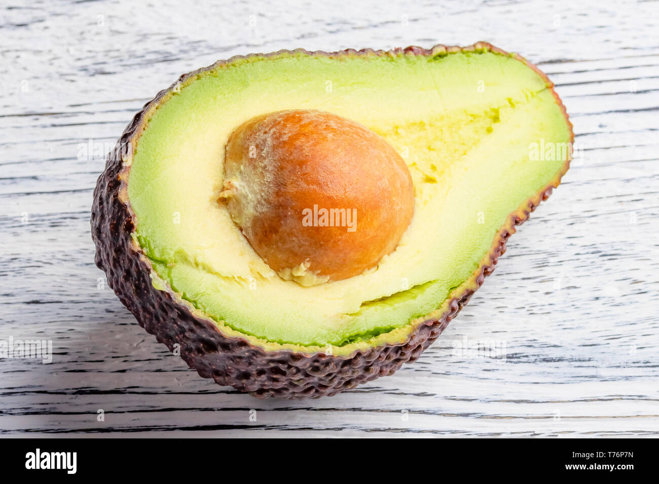 Half a juicy ripe avocado with a round bone and reddish peel on a white ...