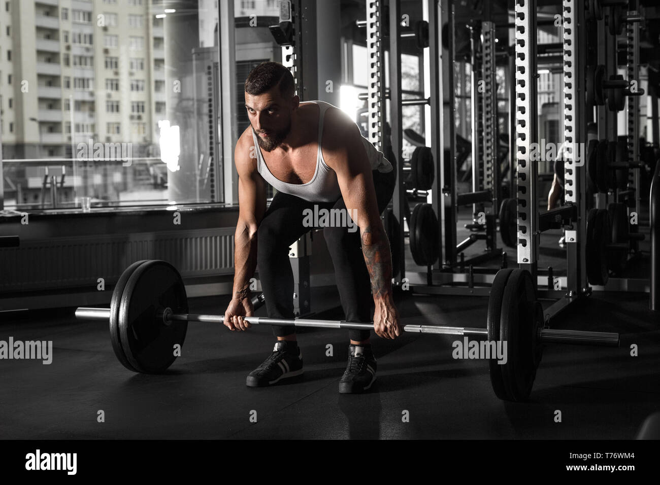 Bearded man bodybuilder exercising at gym bending down holding barbell ...