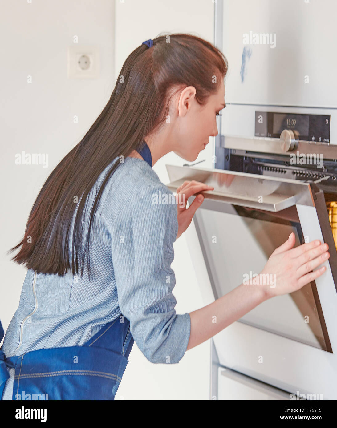 Beautiful woman in the kitchen, waiting with the front of the oven ...