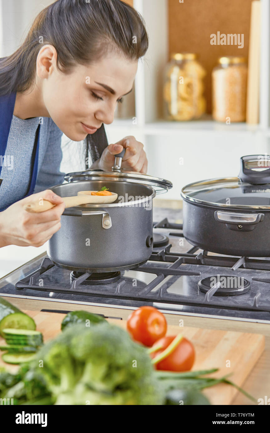 Beautiful girl is tasting food and smiling while cooking in kitchen at ...