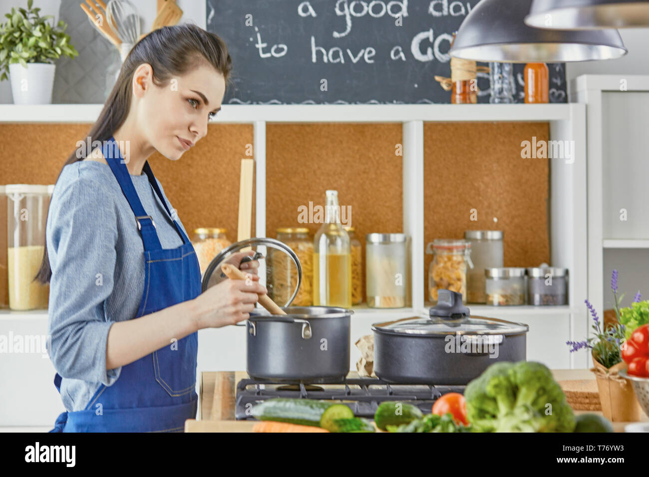 Beautiful girl is tasting food and smiling while cooking in kitchen at ...