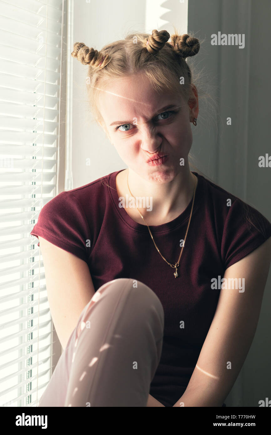 fun angry young woman sitting on window making grimace looking at ...