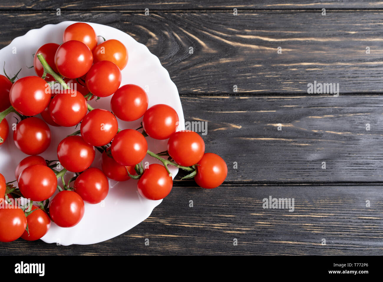 Cherry tomatoes in the white plate on the dark wooden table. Juicy ripe ...