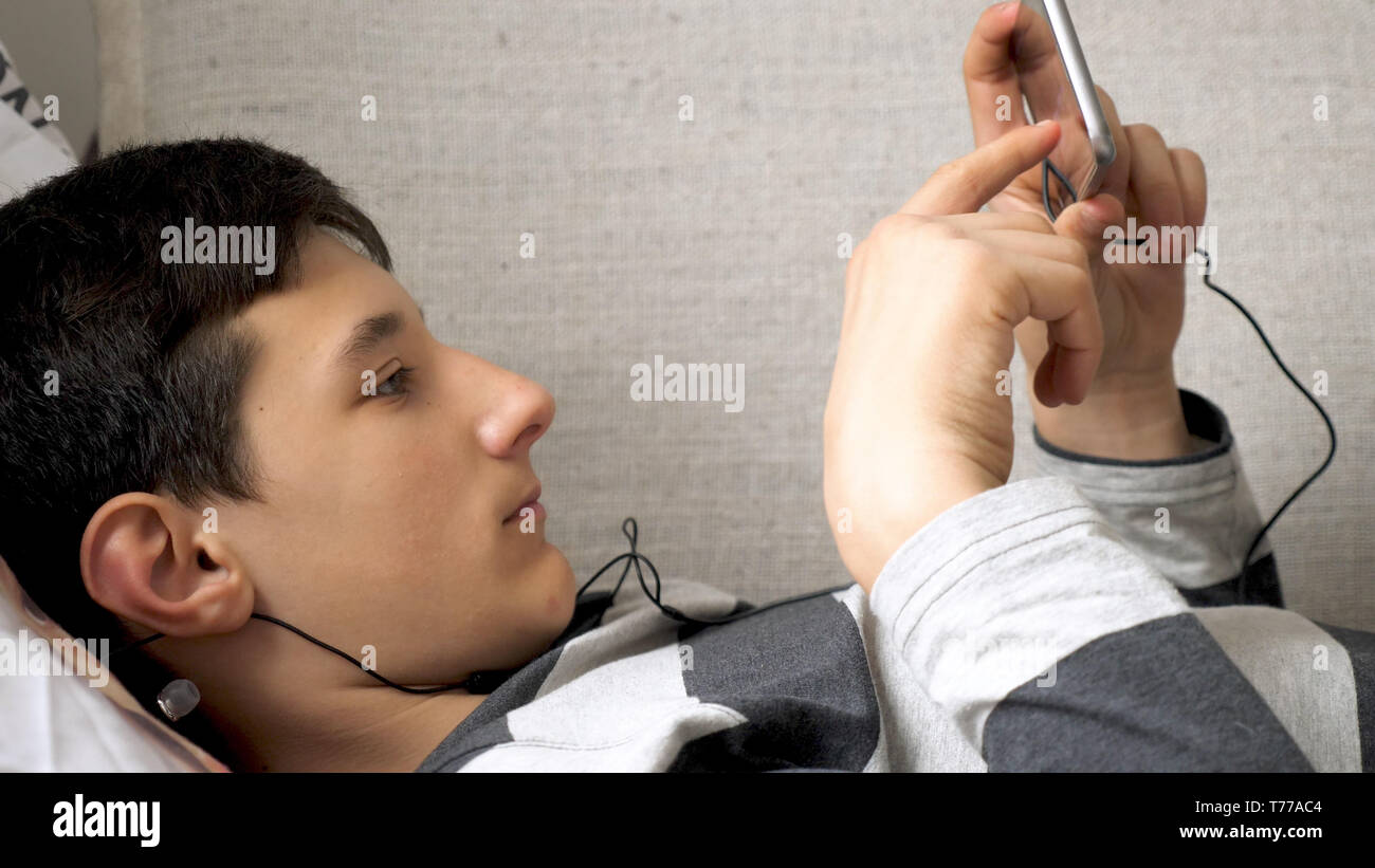 serious teen boy with smart phone listening or talking on sofa indoor ...