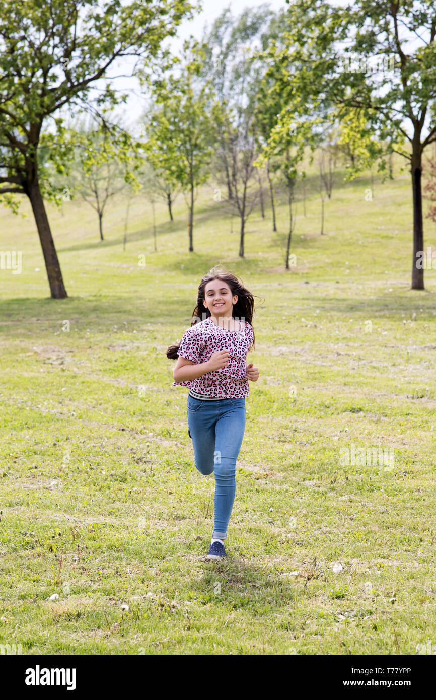 Fit athletic young girl in jeans and sneakers running through a park in ...