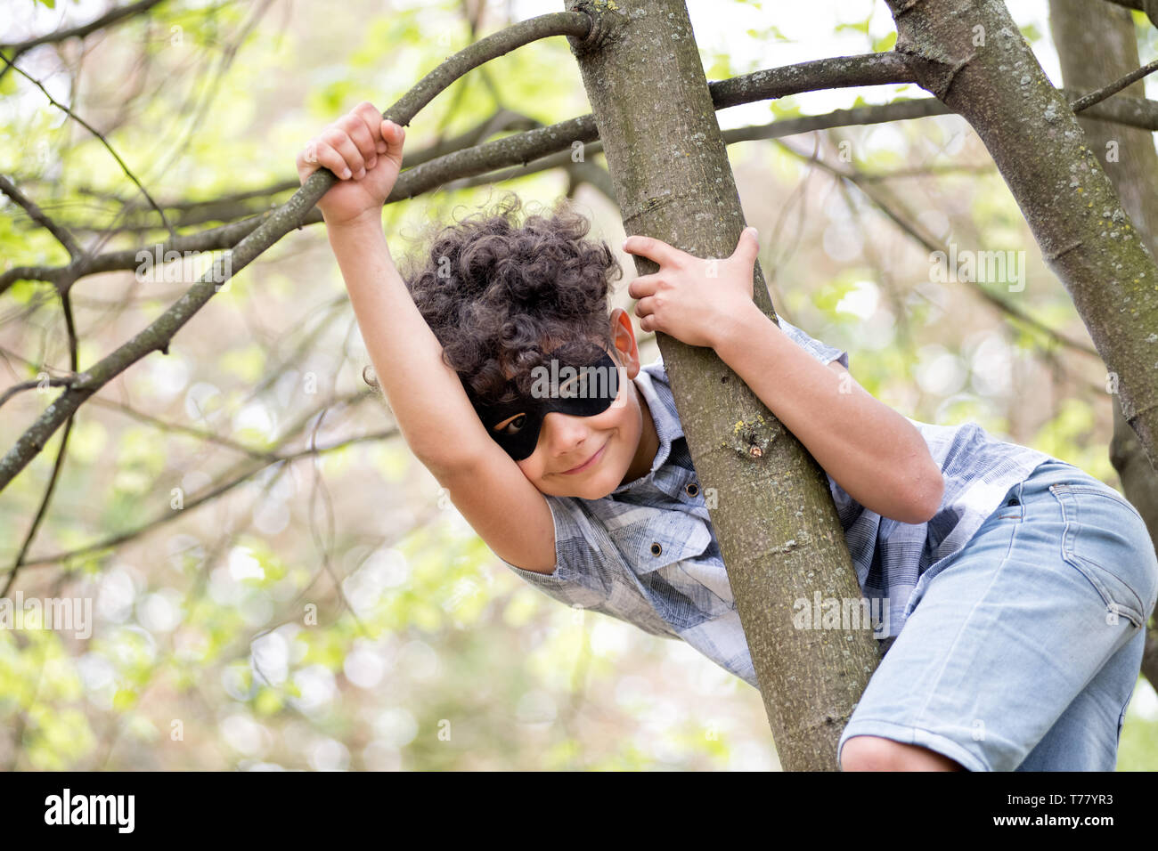 Cute young boy with curly dark hair wearing a mask climbing a tree ...