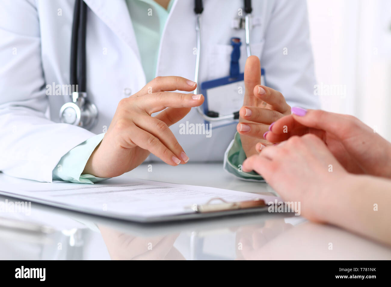 Unknown doctor and patient talking while sitting at the desk in ...