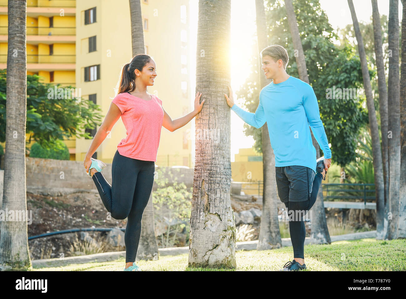 Sporty couple stretching legs leaning on a tree in park at sunset - Two ...