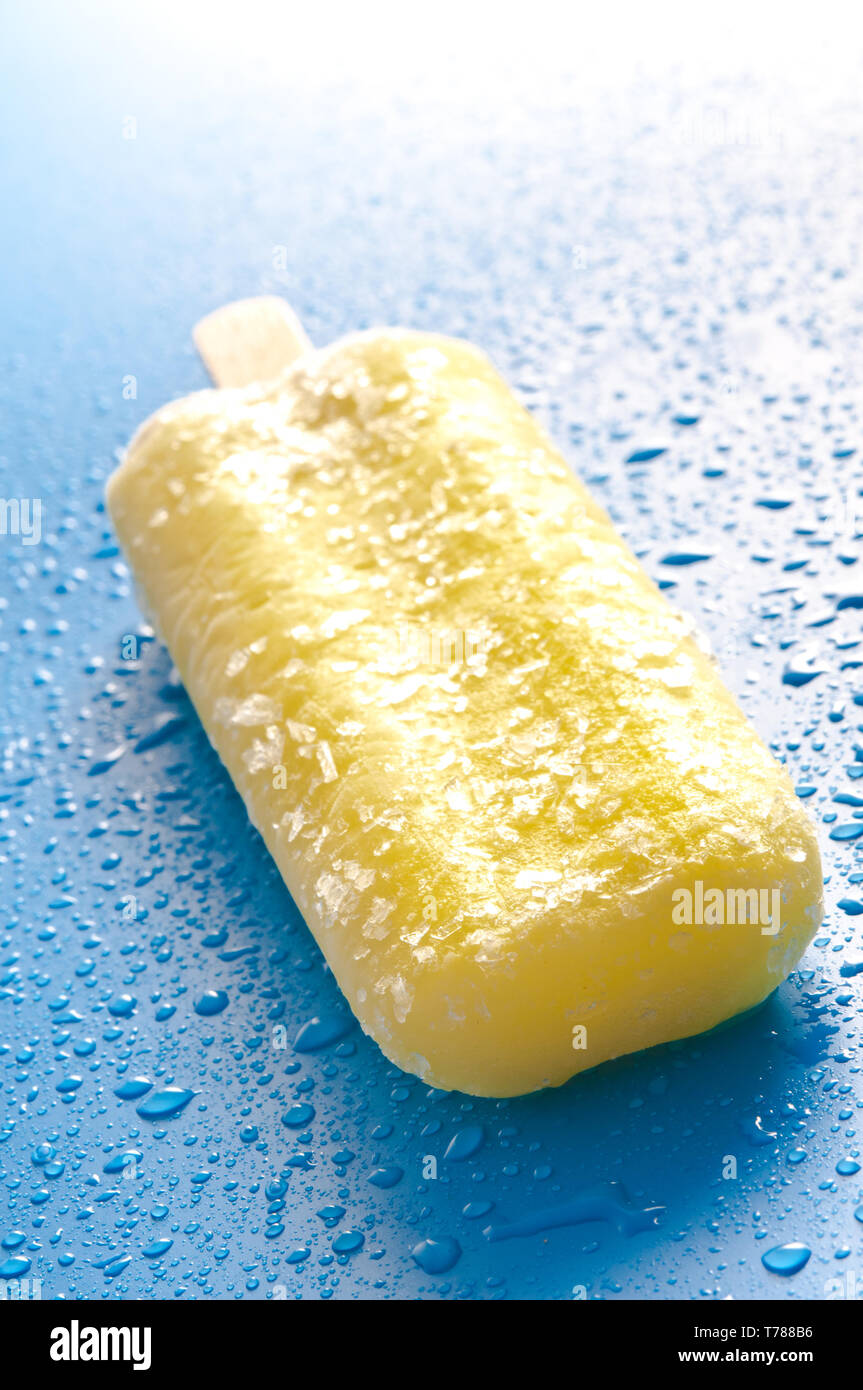 yellow ice lolly or ice pop on a blue background with drops of water ...