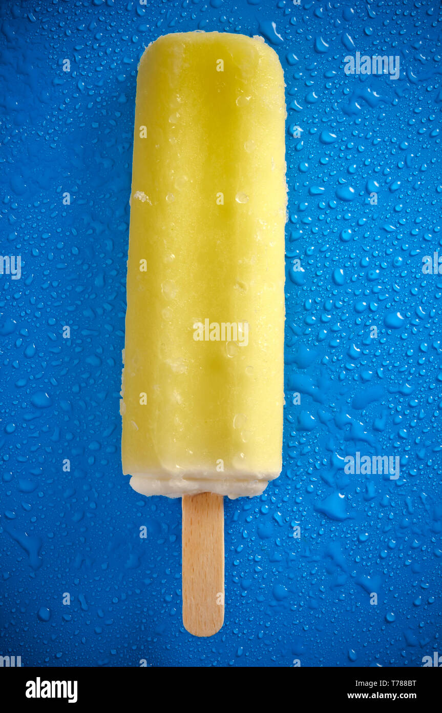 yellow ice lolly or ice pop on a blue background with drops of water ...