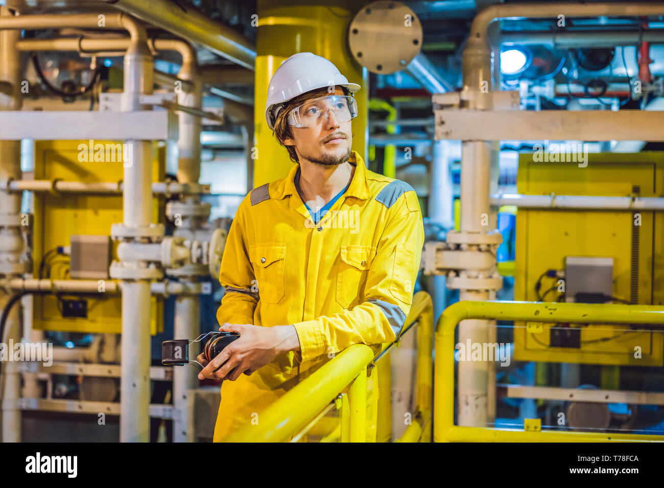 Young man in a yellow work uniform, glasses and helmet in industrial ...