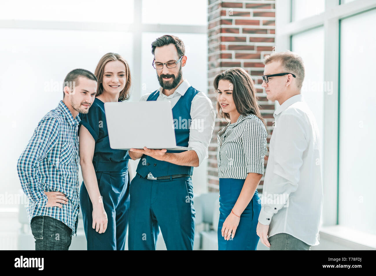 business team looking at laptop screen standing in office lobby ...