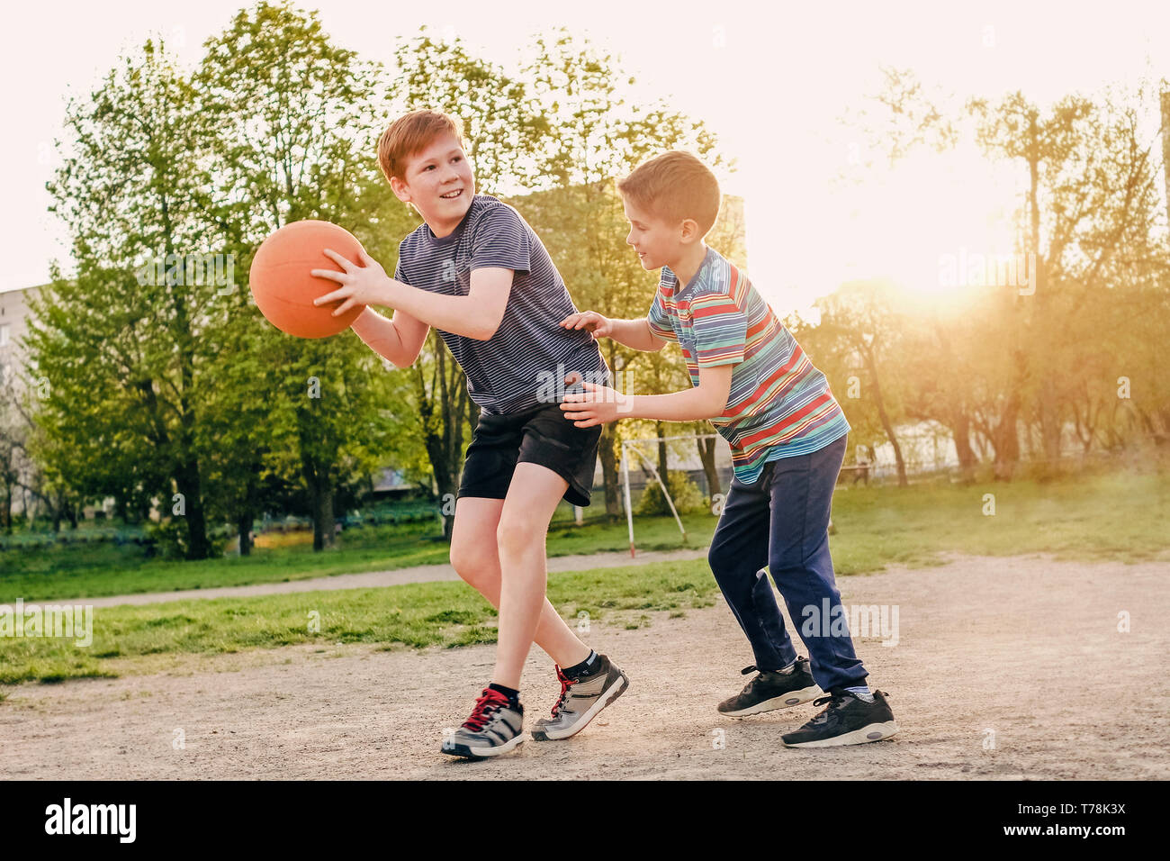 Two happy young boys playing basketball outdoors on a sports field in ...
