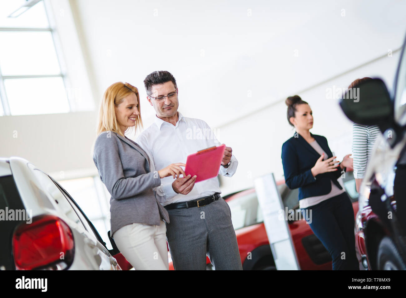 Woman is talking to handsome car dealership worker while choosing a car ...