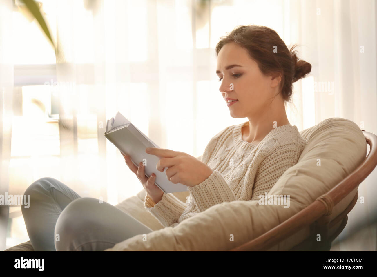 Young woman reading book on lounge chair at home Stock Photo - Alamy