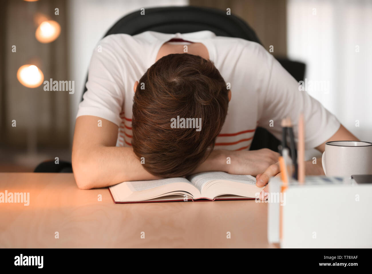 Young man sleeping while sitting at table with book Stock Photo - Alamy