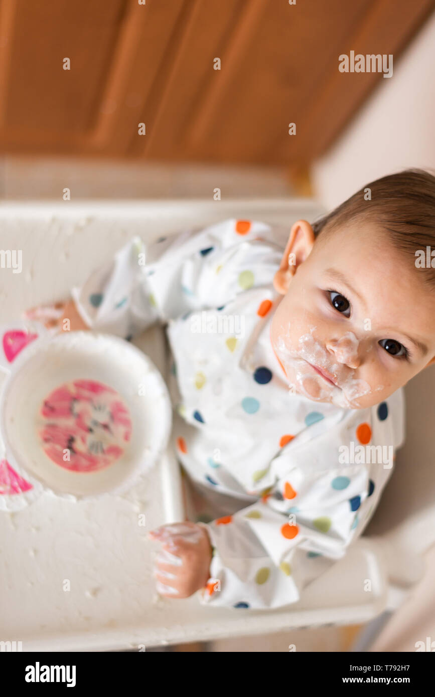 A Little baby eating her dinner and making a mess with yogurt and ...