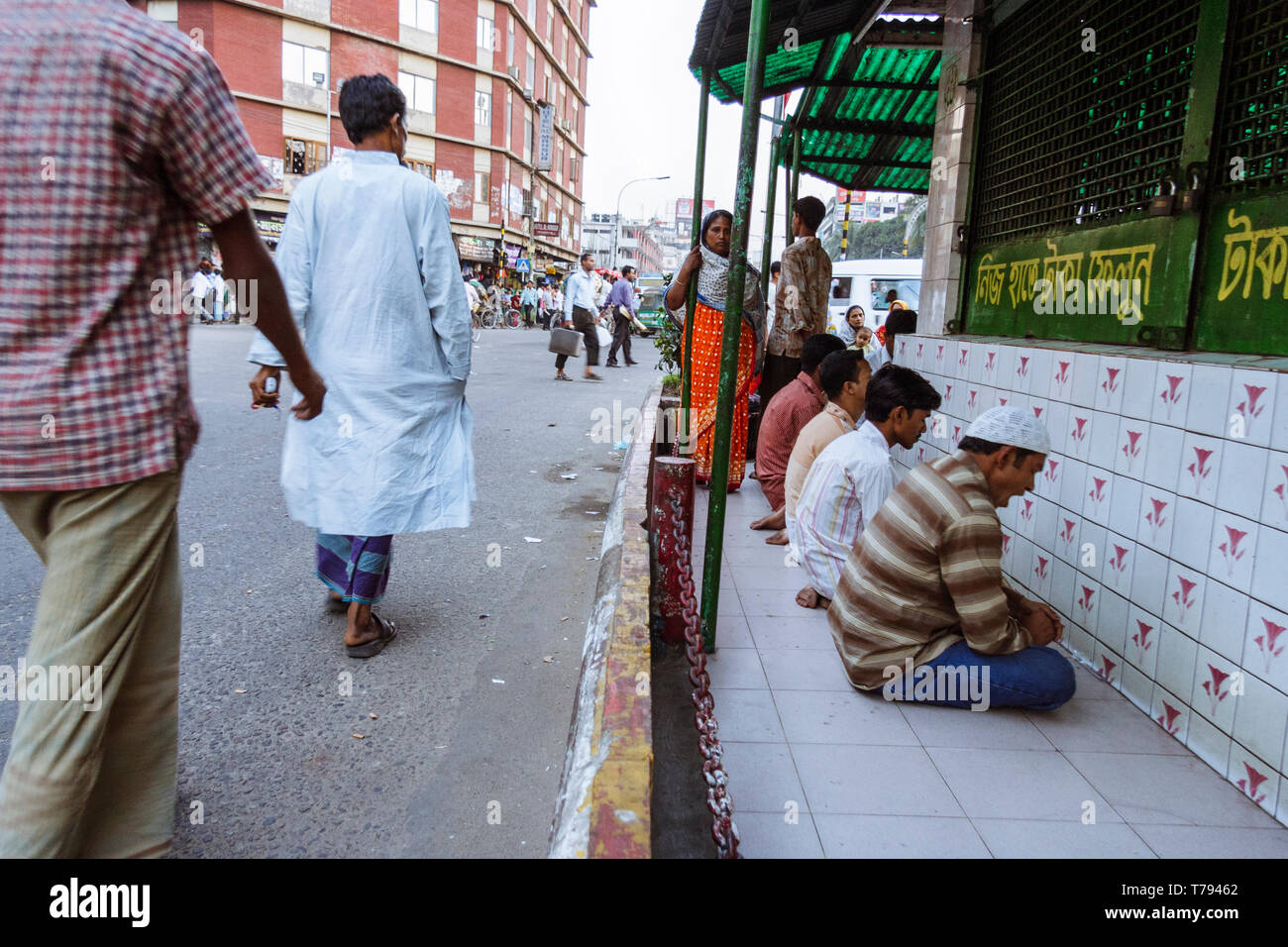 Dhaka, Bangladesh : Pedestrians walk past worshippers praying at the ...