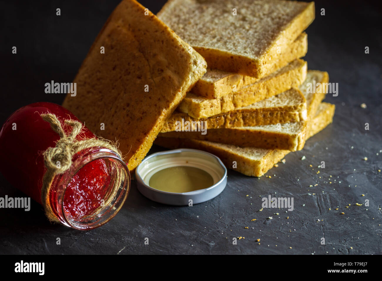 Strawberry jam bottle and whole wheat bread are stacked on a black ...