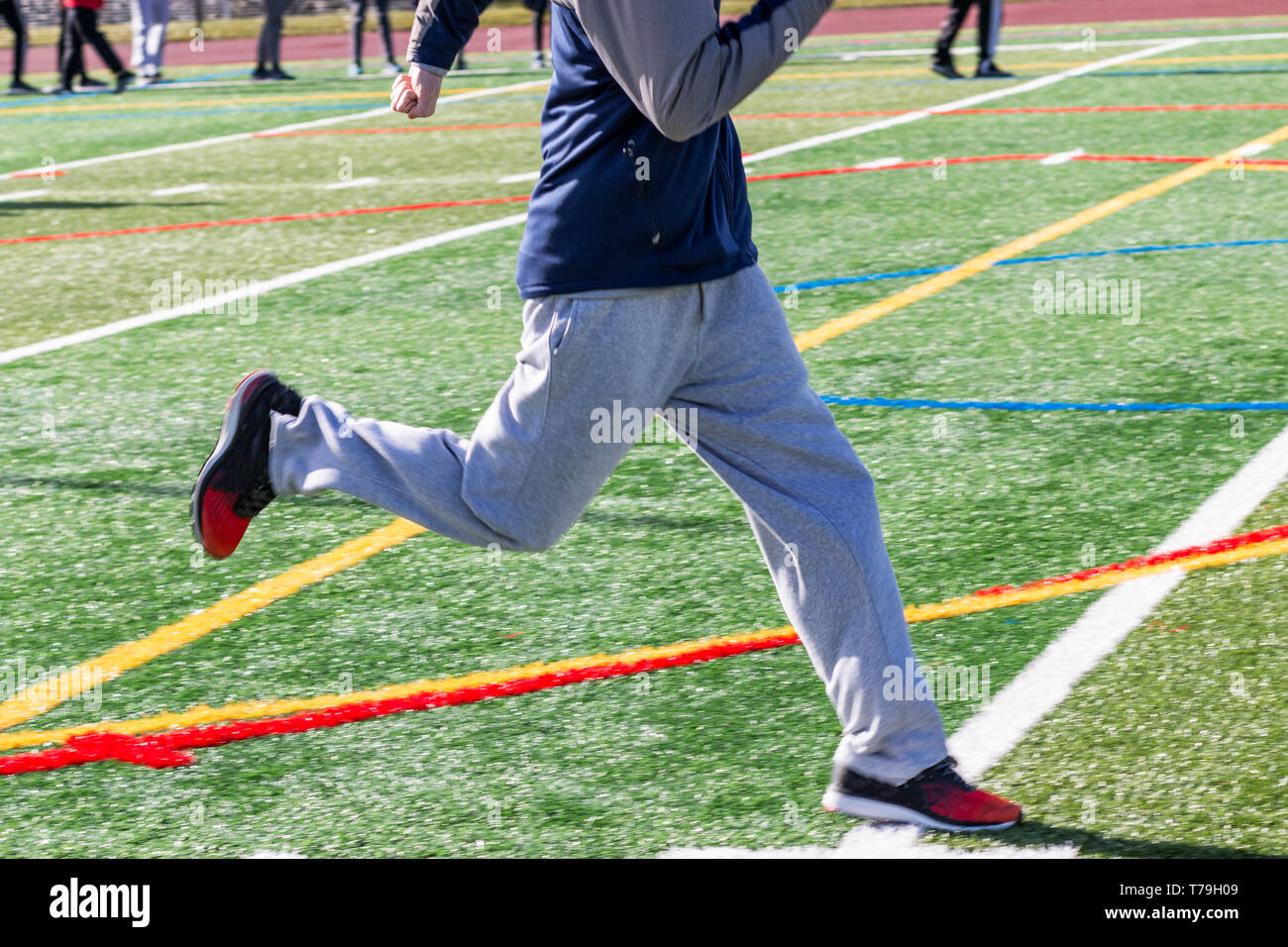 A high school sprinter is running on a green turf field during winter ...