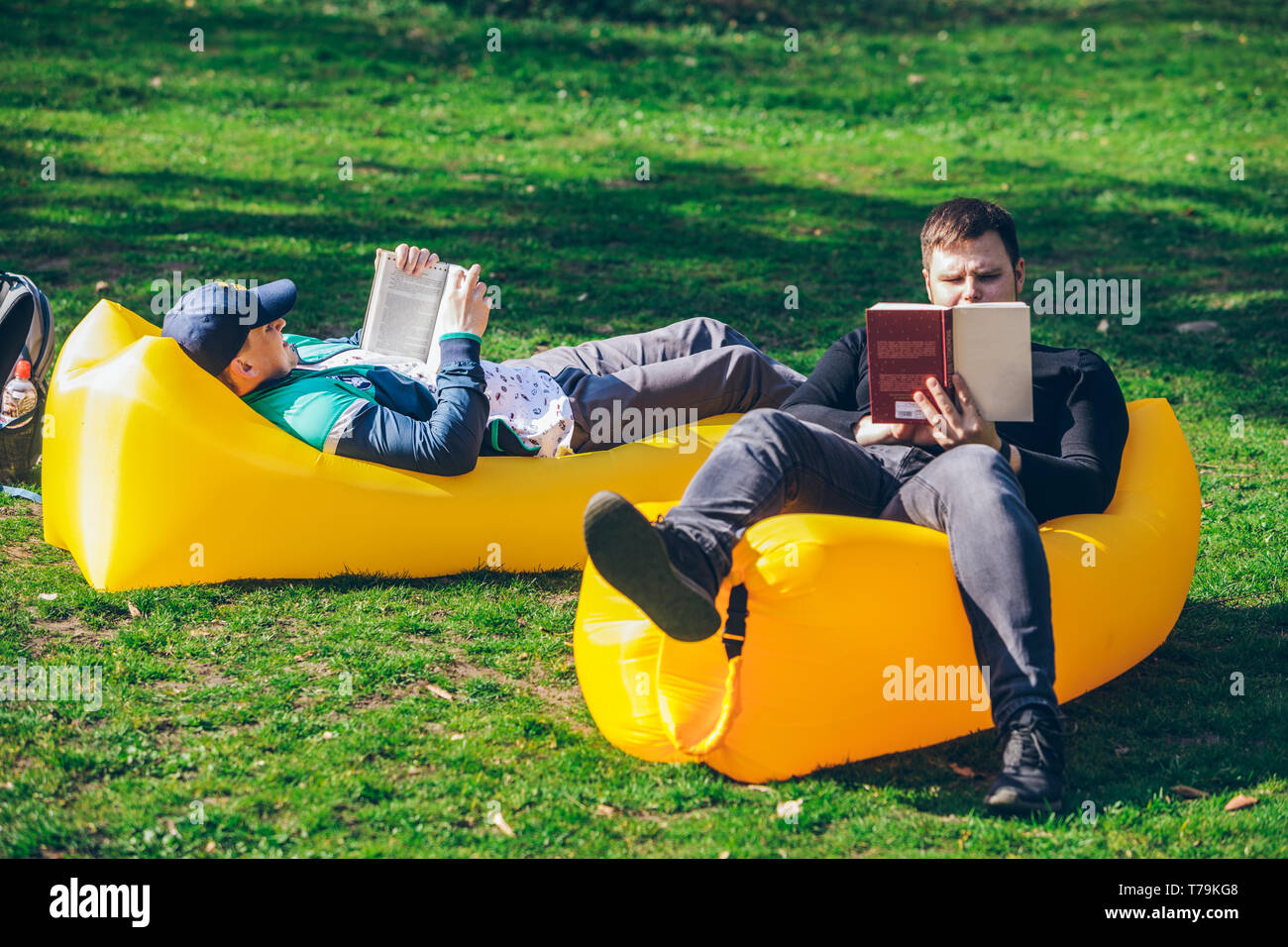 two men friends laying on yellow inflatable mattress reading books ...