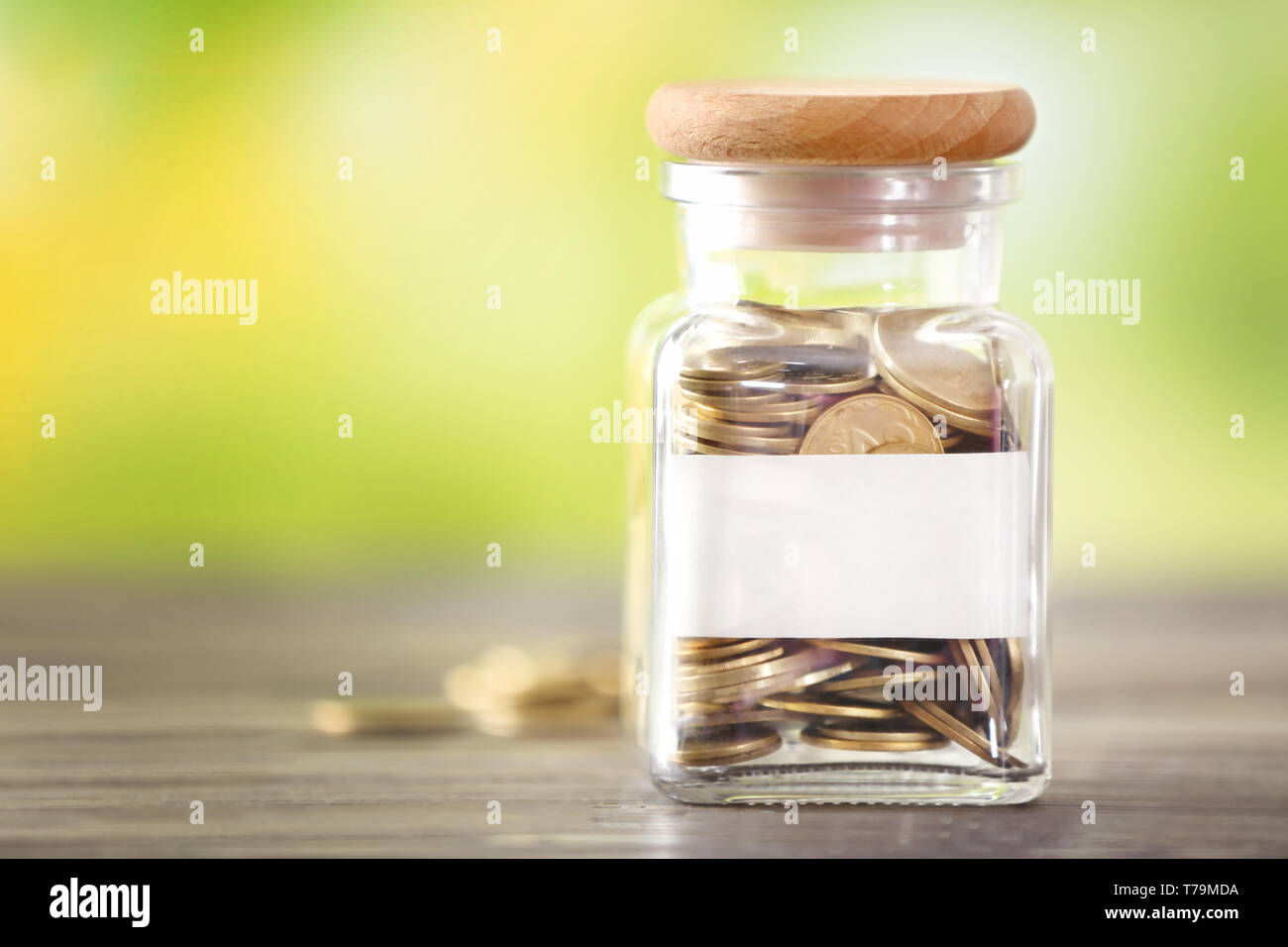 Glass jar with coins and label on table against blurred background ...