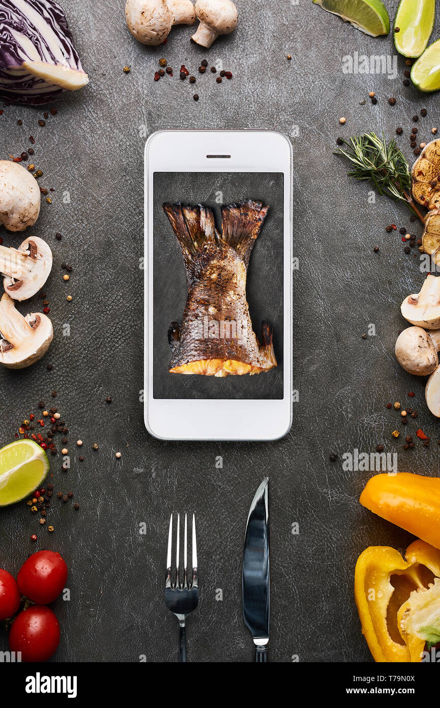 creative food concept with roasted fish tail in smartphone display ...
