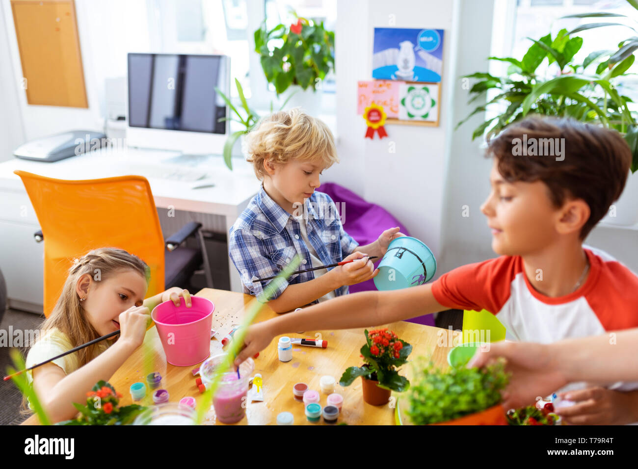 Coloring buckets. Three cute pupils feeling busy and interested while ...