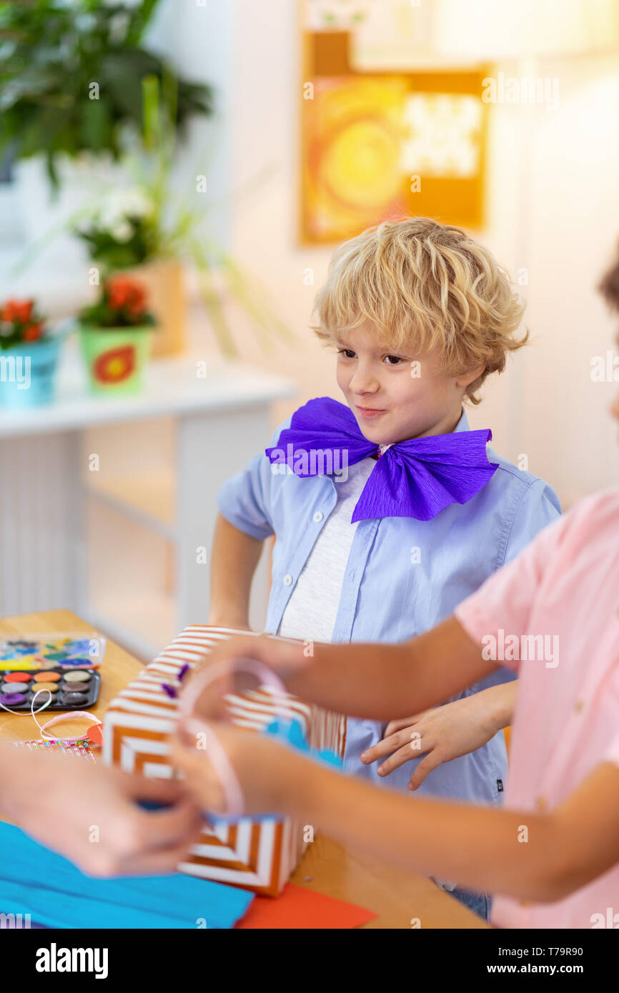 Blue paper bow. Cheerful blonde-haired schoolboy wearing blue paper bow ...
