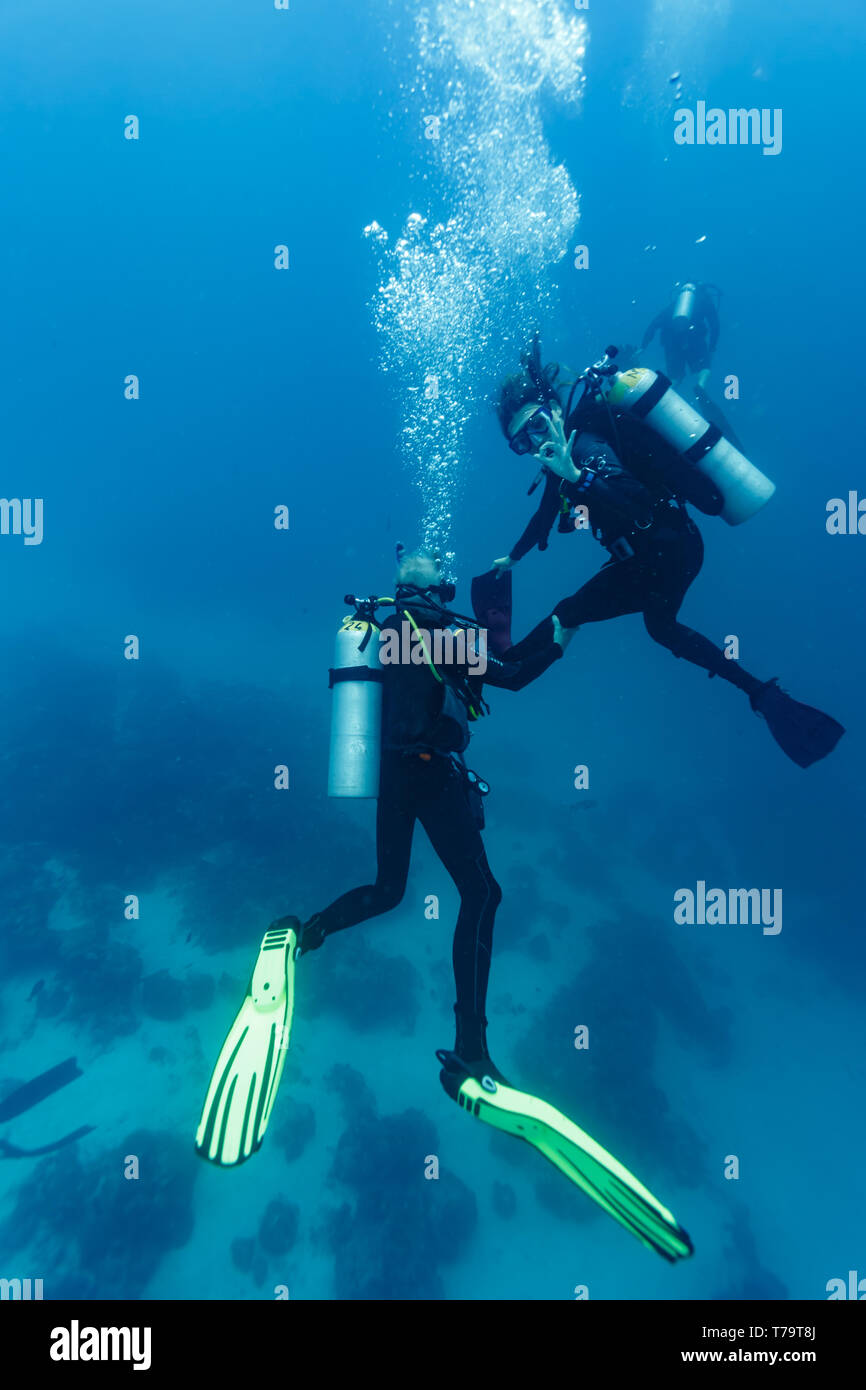 Closeup of two scuba divers descending into turquoise tropical waters ...