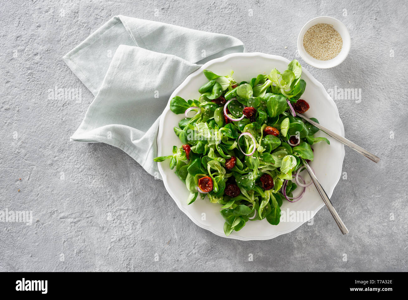 Bowl of green salad with mache leaves and baked tomatoes on concrete ...