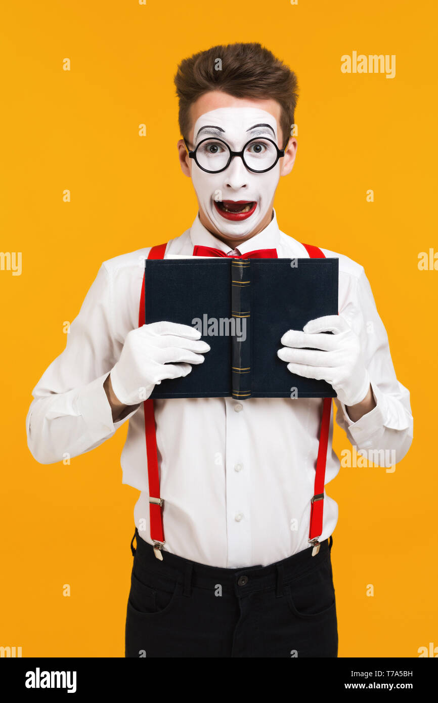 portrait of surprised mime man artist reading book isolated on yellow ...