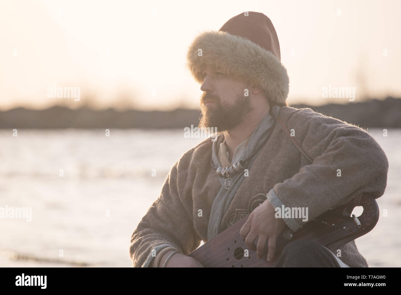 Man reencator in national costume playing gusli ancient traditional ...