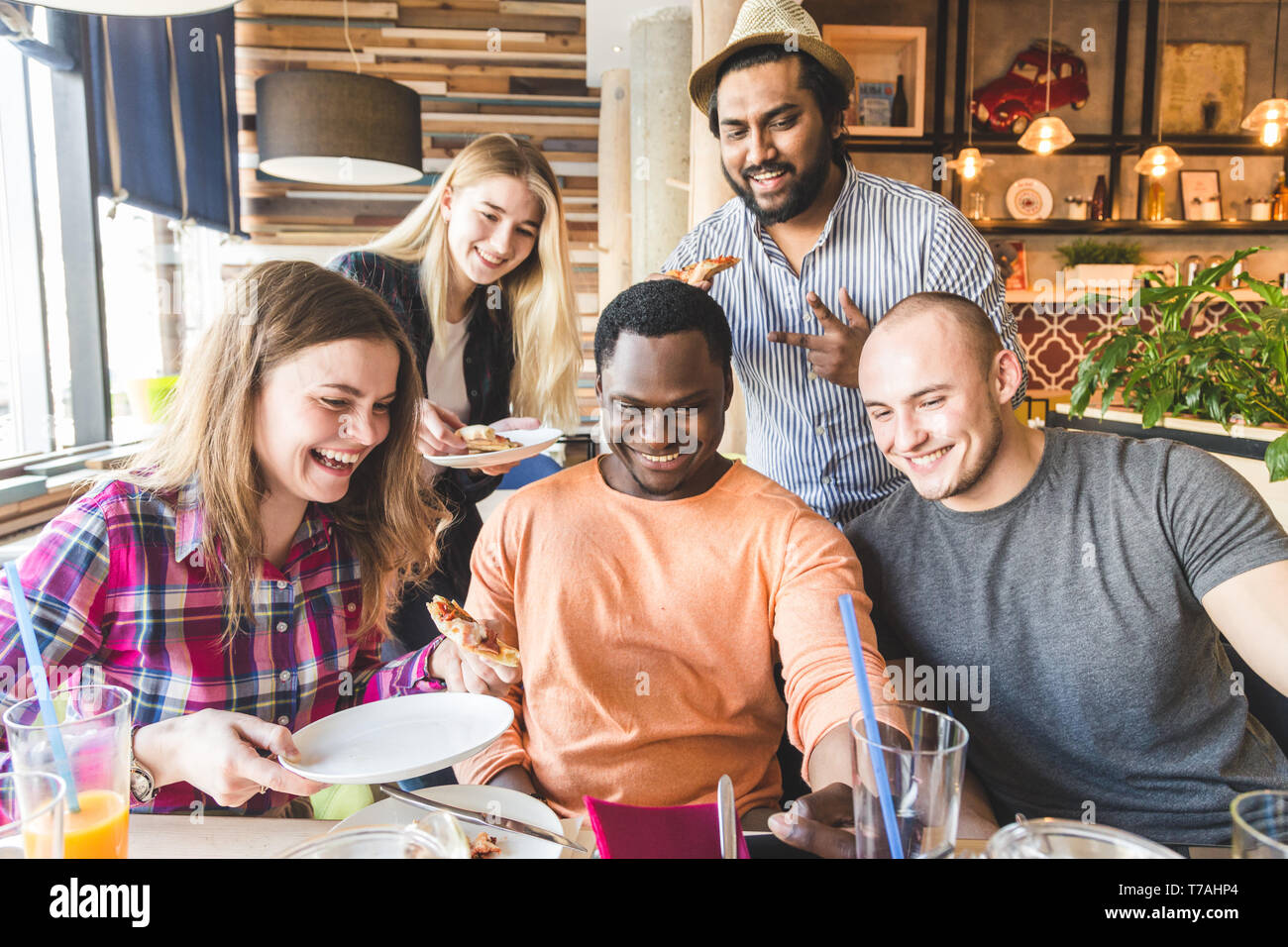 A company of multicultural young people in a cafe eating pizza ...