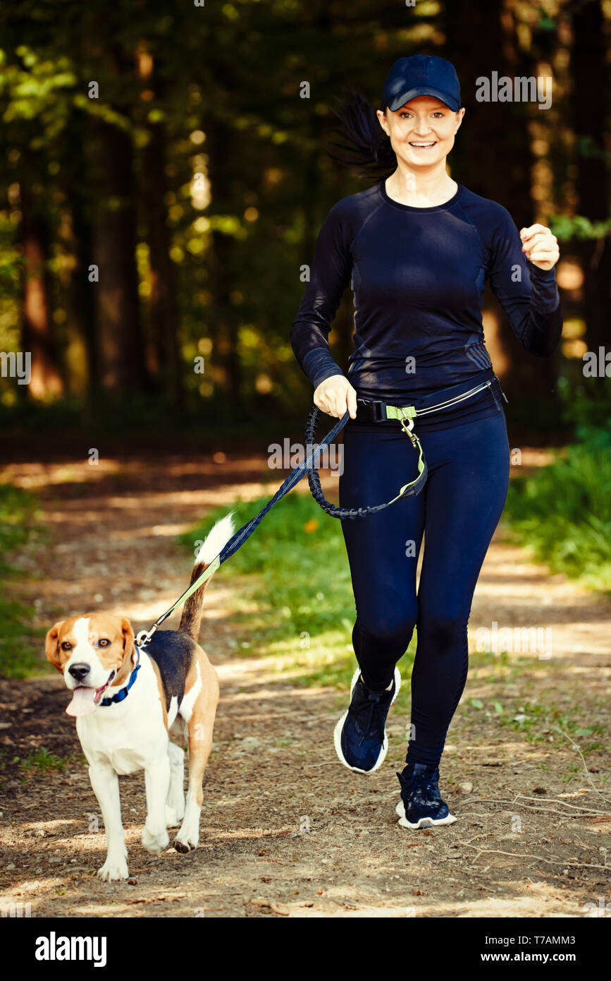 Girl running with dog outdoors in nature on a path in forest. Sunny day ...