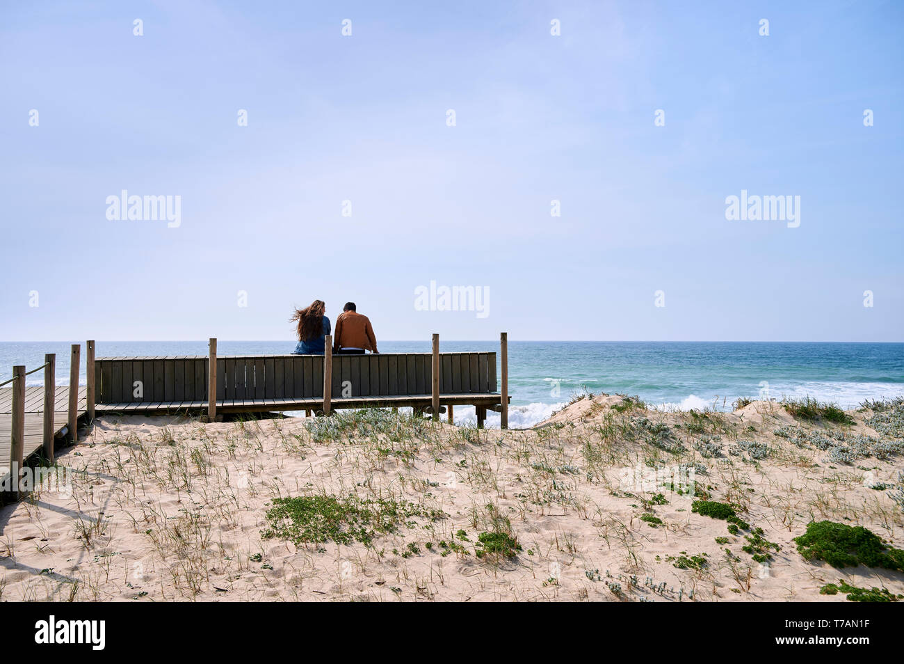 Young couple seated on a bench watching the ocean with the wind on ...
