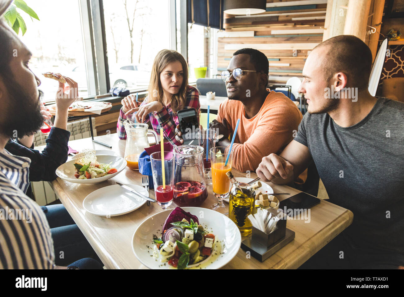 A company of multicultural young people in a cafe eating pizza ...