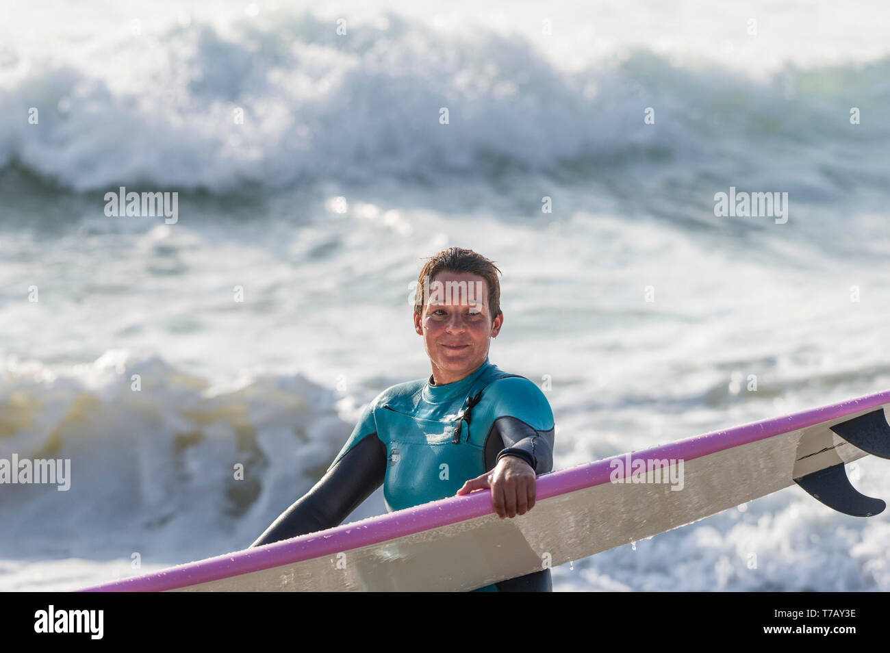 A female surfer carrying her surfboard on Fistral Beach in Newquay in ...