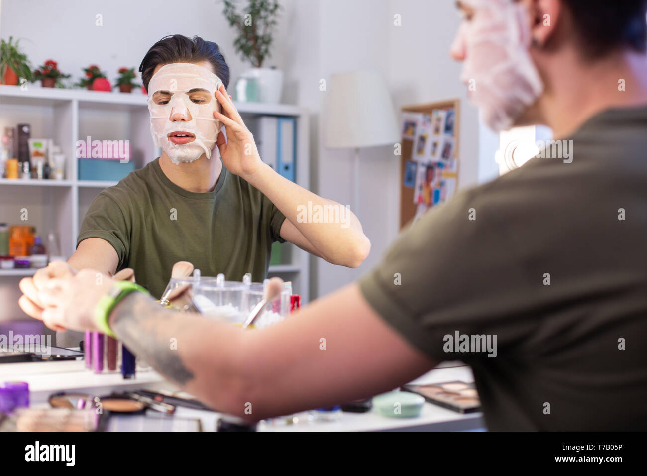 Curious man in green t-shirt touching his new face mask Stock Photo - Alamy