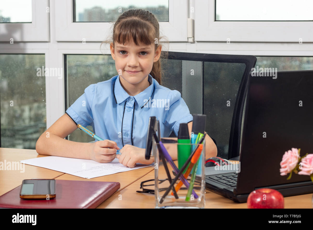 A girl of eight years old at the table in the office plays in the ...