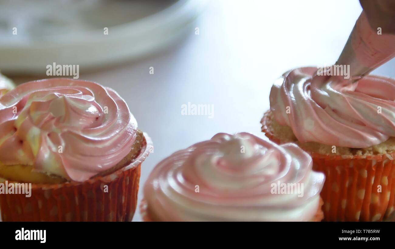 Decorating cup-cake with cream. Using cooking bag, confectioner making ...
