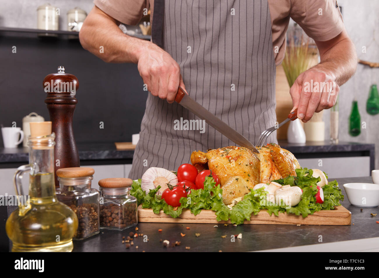 Hands of chief man cuting baked chicken with vegetables with a big ...