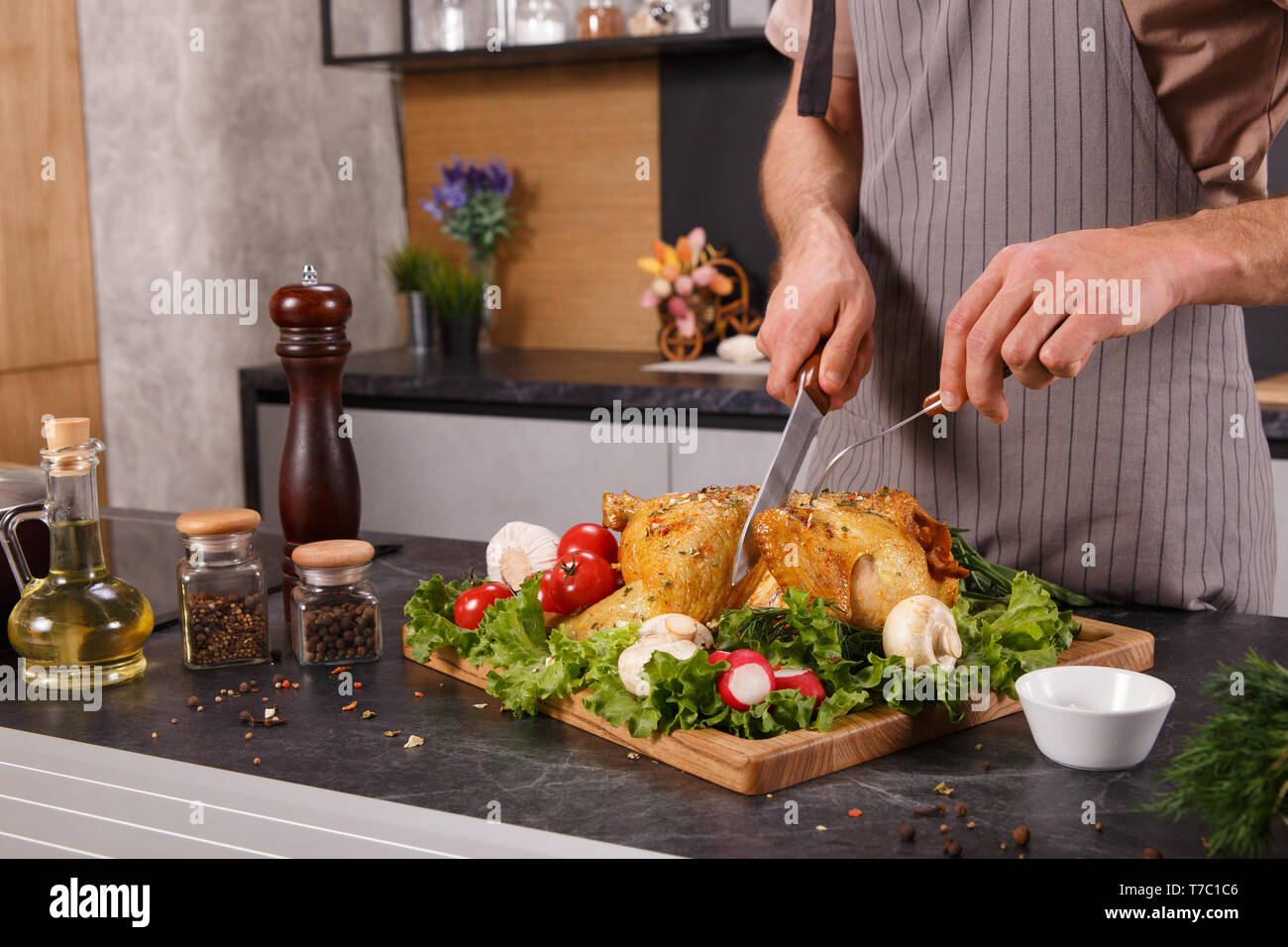 Hands of chief man cuting baked chicken with vegetables with a big ...