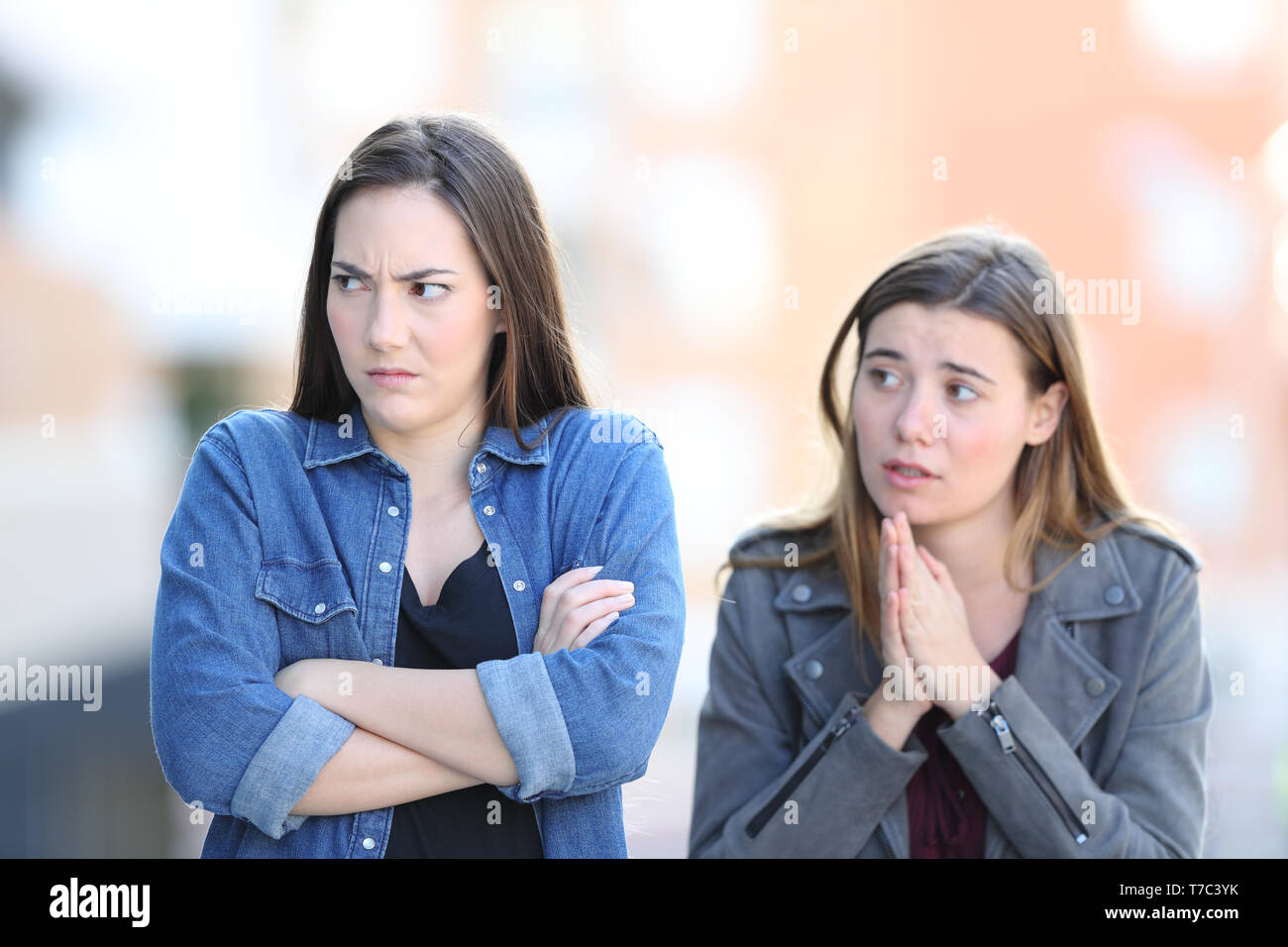 Front view of a regretful girl asking forgiveness to her angry friend ...