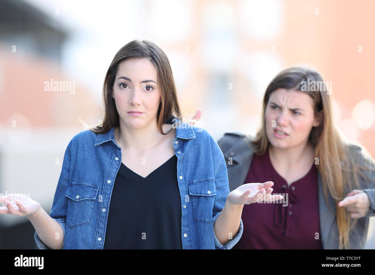 Front view portrait of a woman scolding her confused friend who looks ...