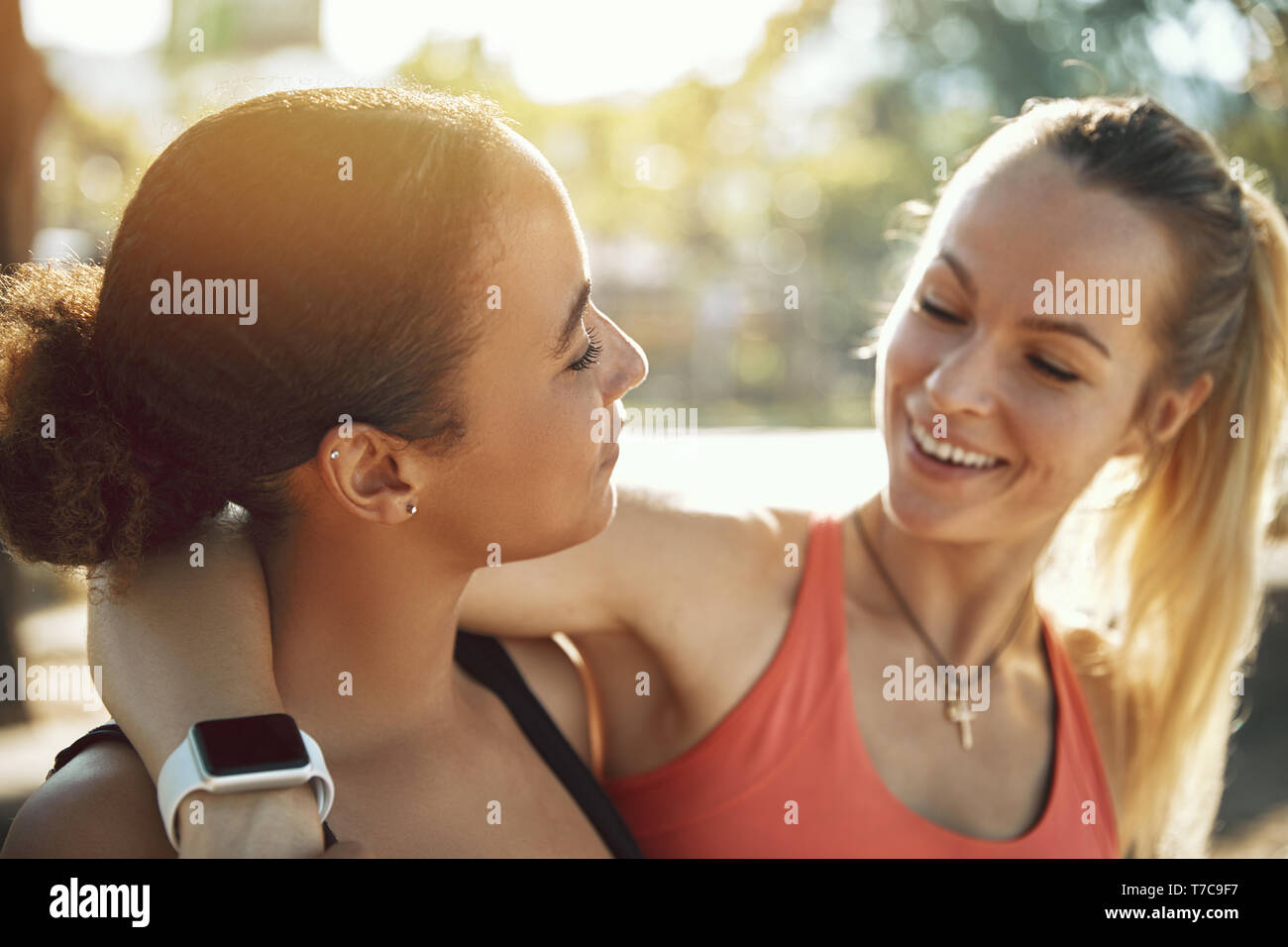Two fit young women in sportswear laughing while standing arm in arm ...