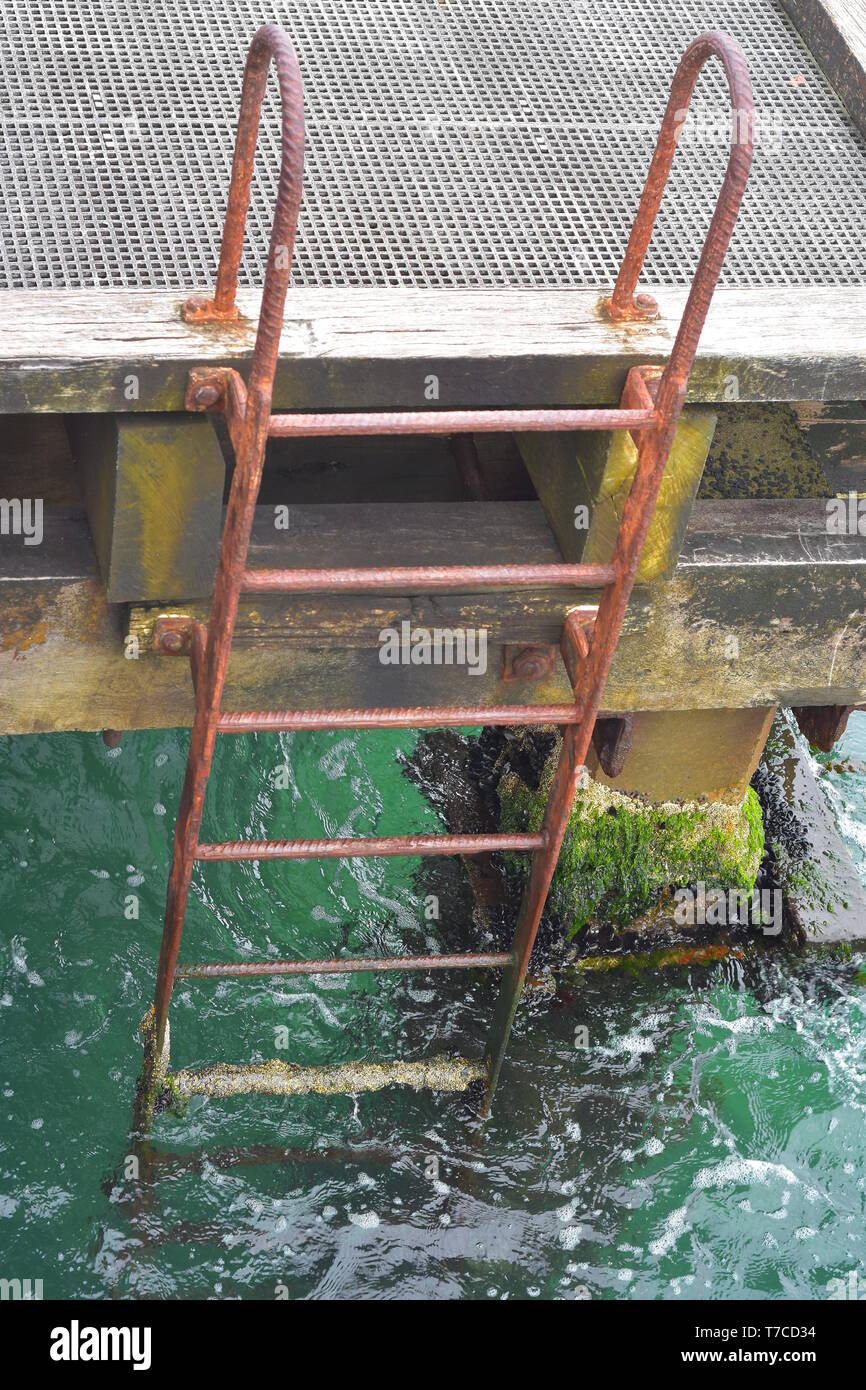 Welded rusty iron ladder bolted to wharf made of timber platform and ...
