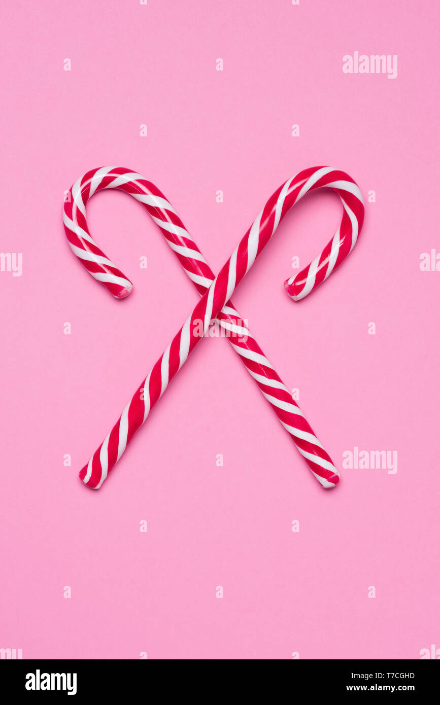 Shiny red and white traditional candy canes crossed on pink background ...